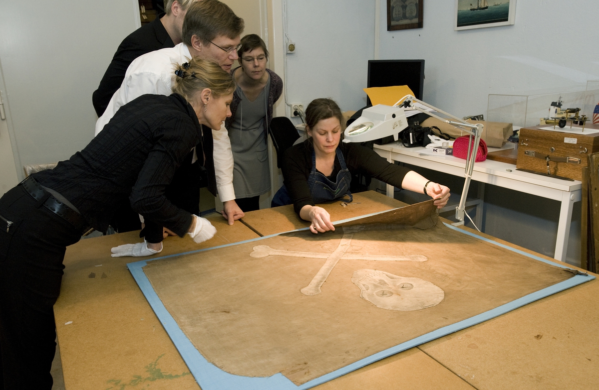 Konservator från Armémuseum tittar till en inlånad piratflagga från ...