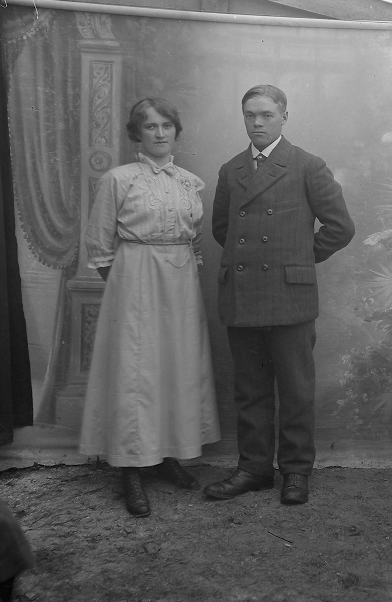 Portrett. Par i 20-30-åra. Står. Dress og finkjole.Bildet er tatt i ...