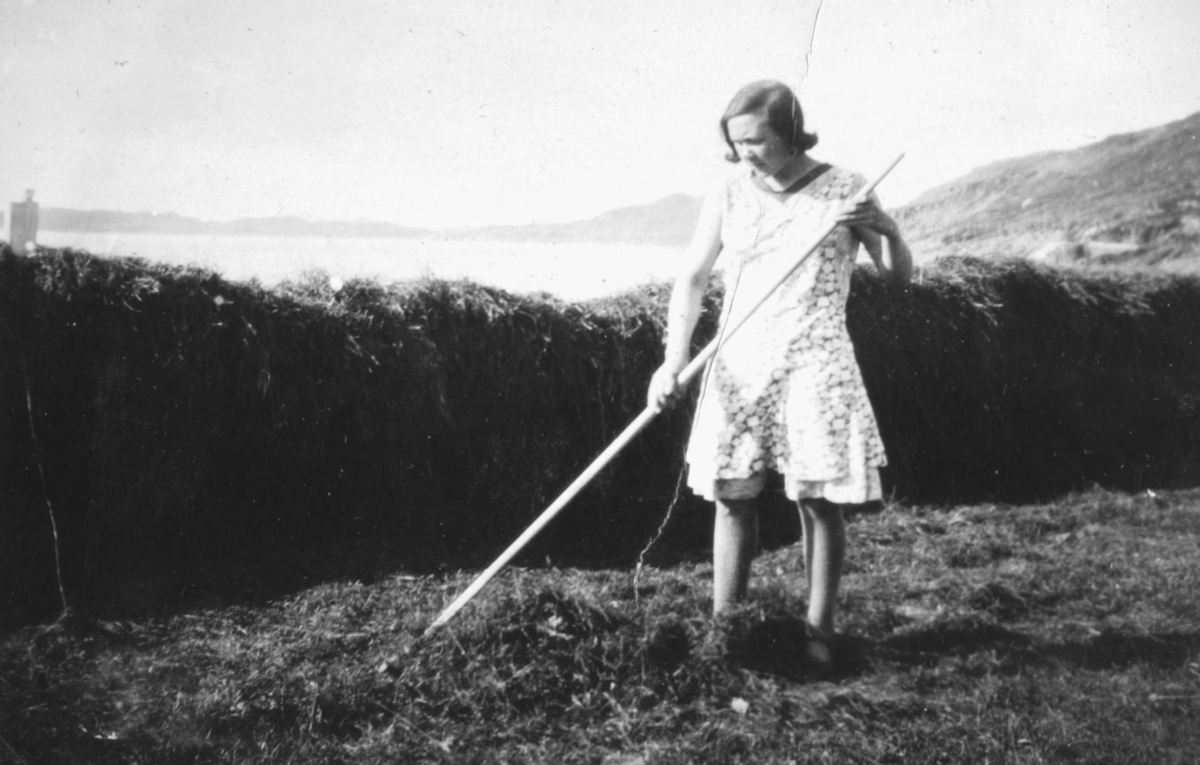 En dame på et jorde med en rive i hendene. Personen er ukjent og bildet ...