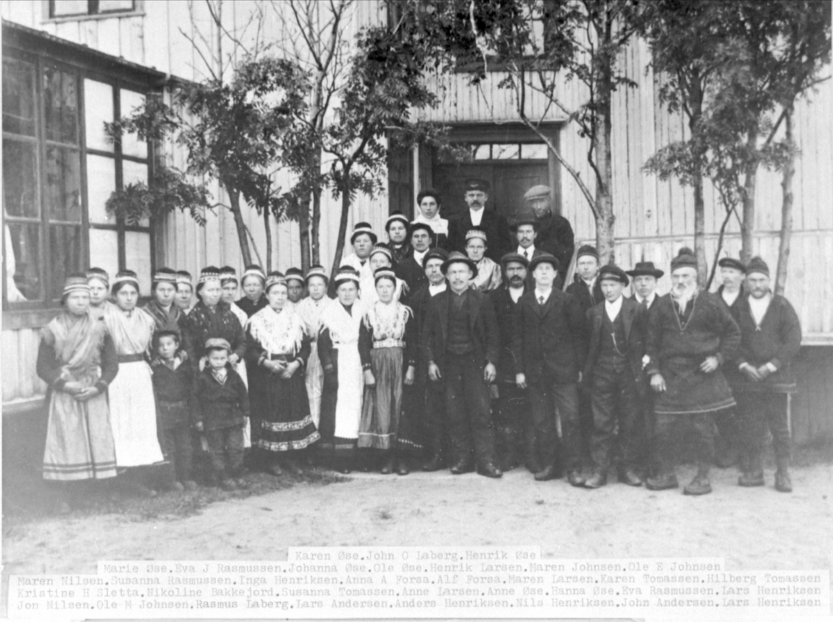 Gruppeportrett tatt foran et større bygg. Flere av gjestene har samisk ...