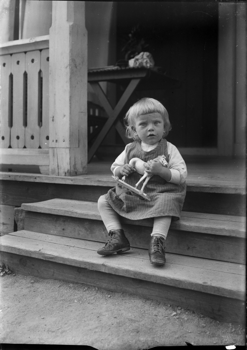 Litet barn sitter på trappa med en leksakshäst i famnen ...