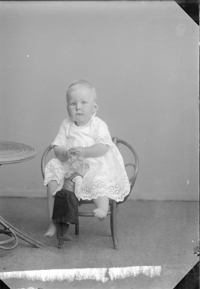 Ett litet barn sitter i en liten stol med en docka i händerna. - Grenna ...