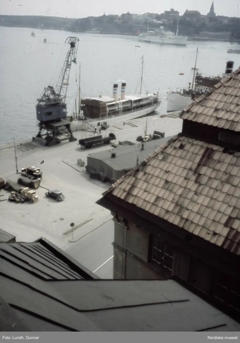 Skeppsbron i Stockholm. Lastkran och båtar. Fotografiet är taget från ...