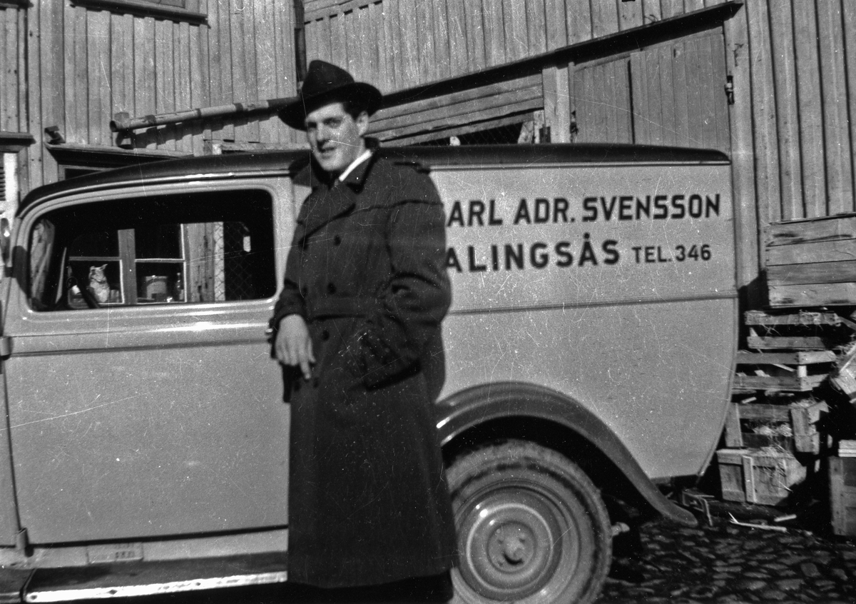 Fotograf Gunnar Persson, iklädd hatt och trenchoat, vid varubilen till ...